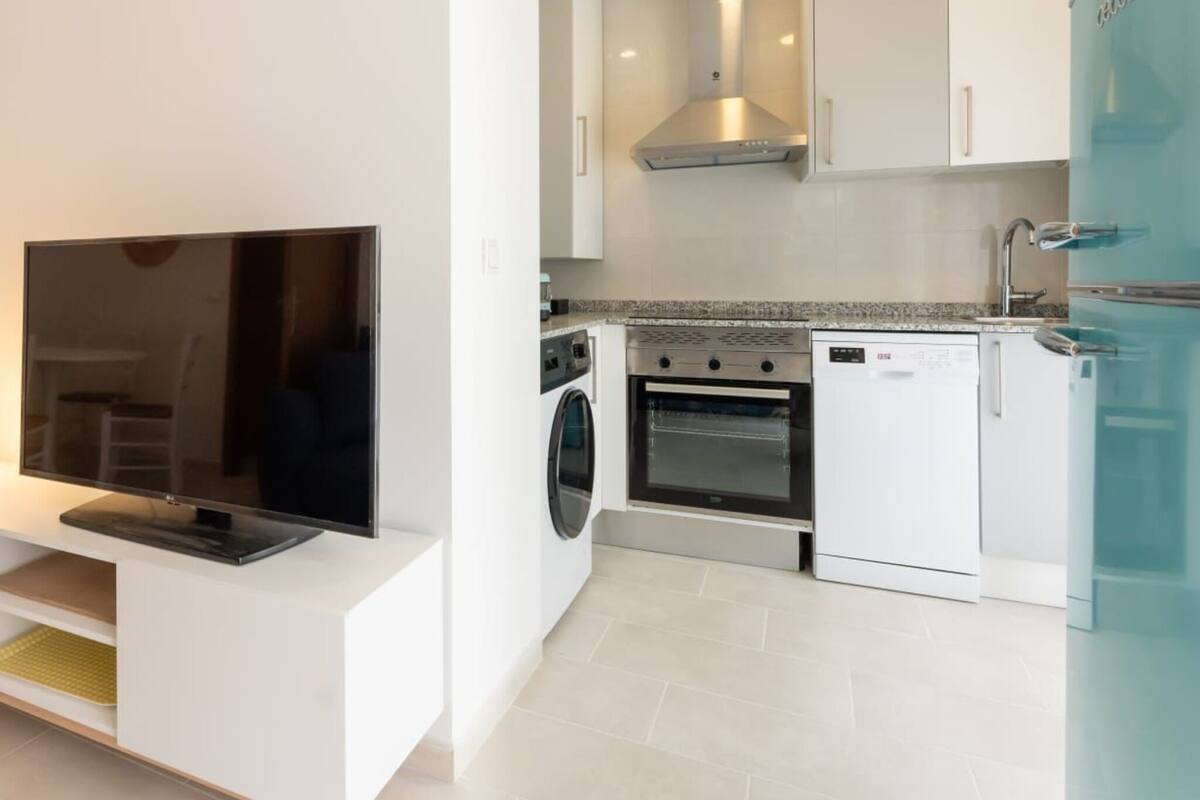 Uma cozinha moderna com televisão de tela plana, forno embutido, máquina de lavar e uma geladeira azul.