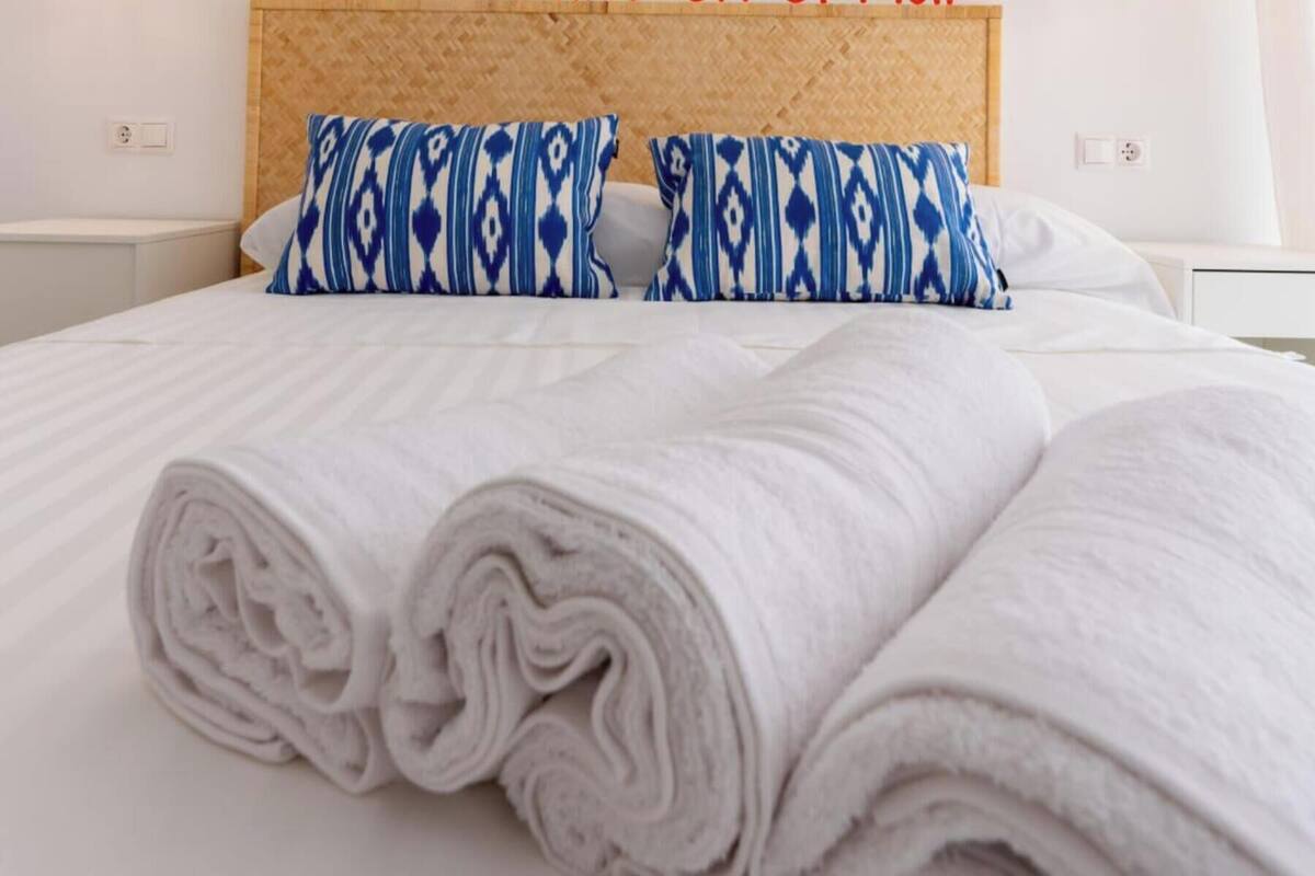 Cama bem arrumada com toalhas brancas dobradas, um painel de cabeceira estampado e um ambiente limpo e funcional.