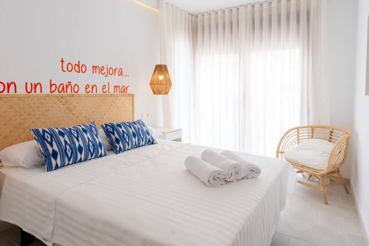 Quarto de hotel com cama, cadeira, luminária e janela com cortinas.