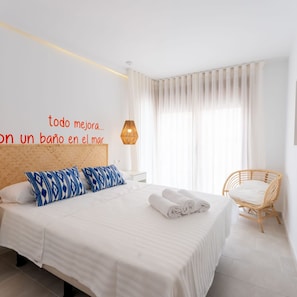 Quarto de hotel com cama, cadeira, luminária e janela com cortinas.