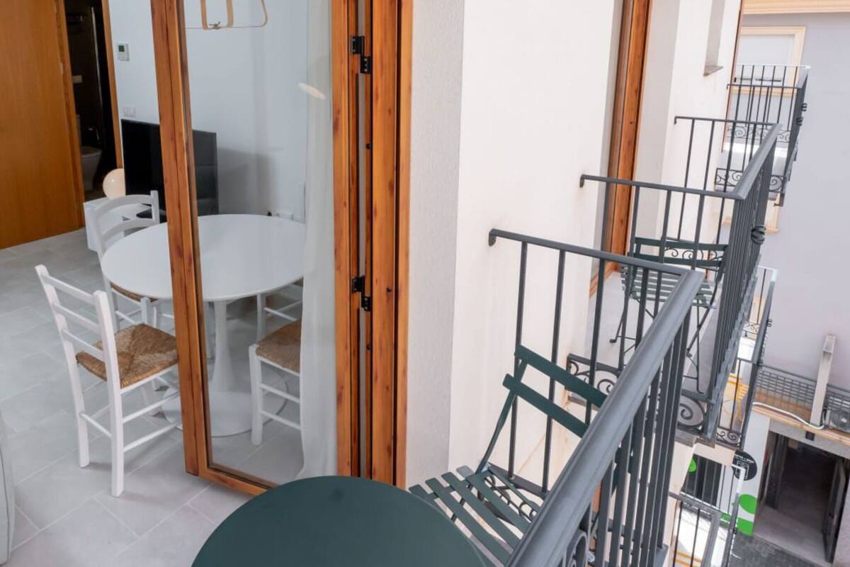 Uma sala de jantar com uma mesa redonda e cadeiras, uma porta de vidro deslizante que dá para outro cômodo, e uma escada com corrimão de metal.