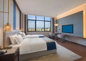 Quarto de hotel com cama grande, escrivaninha, cadeira, televisão e vista para a cidade.