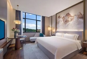 Quarto de hotel moderno com uma cama grande, uma escrivaninha com cadeira, televisão e uma janela ampla com vista para as montanhas.