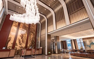 Um hall moderno com balcão de recepção, um candelabro e um mural na parede.