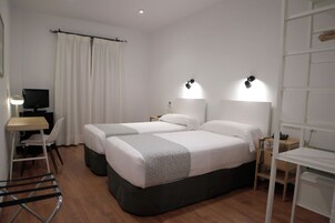 Quarto de hotel com duas camas, uma escrivaninha, uma cadeira, uma televisão e uma mesinha.