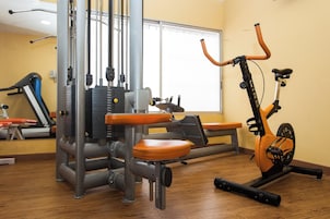 Uma academia com equipamentos de ginástica, uma máquina de remo e uma janela com persianas.