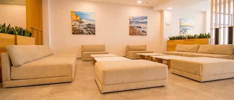 Uma sala de estar moderna com sofás e pufes dispostos ao redor de uma mesa de centro, com obras de arte nas paredes e uma divisória de madeira de um lado.
