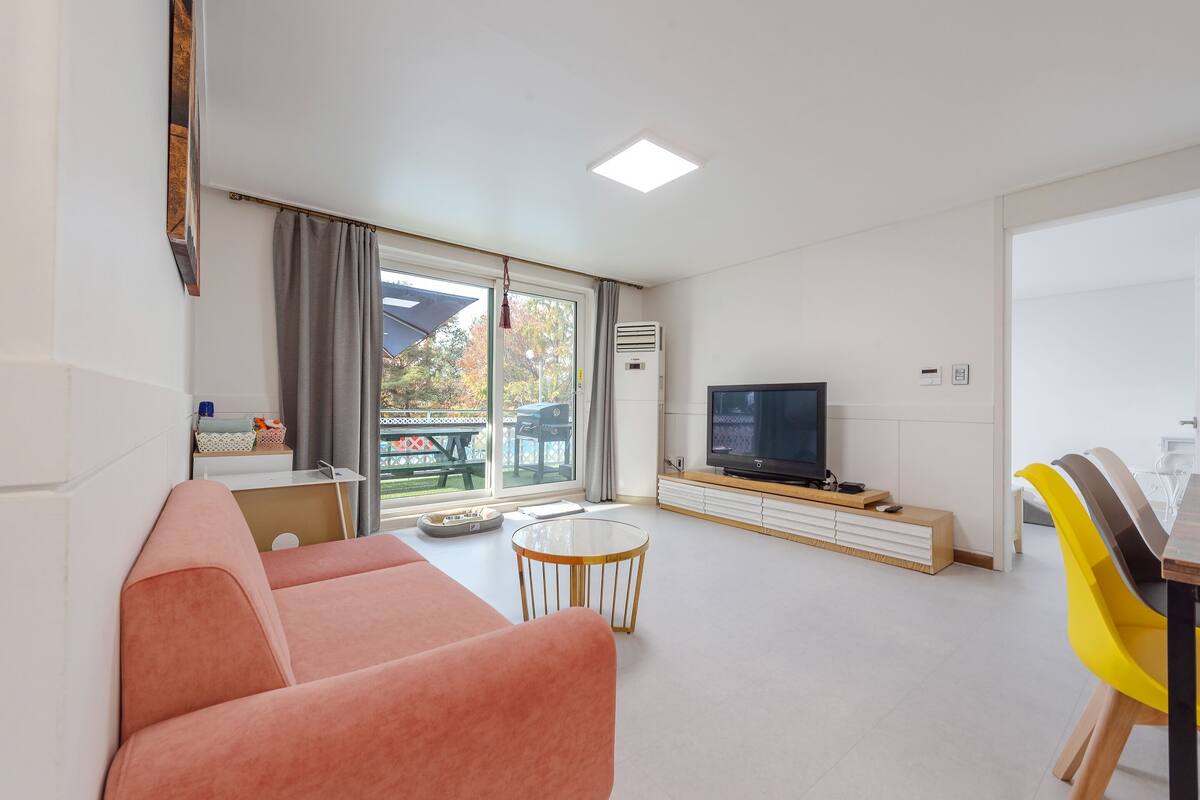 Uma sala de estar moderna com sofá, televisão, mesa de centro e área de jantar com cadeiras.