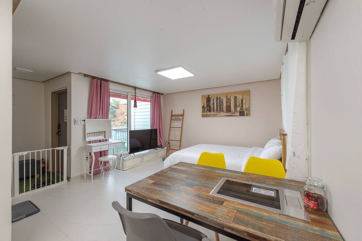 Quarto com cama, escrivaninha, cadeira, televisão e janela com cortinas.