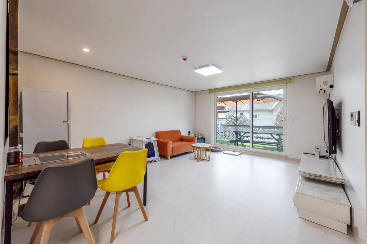 Uma sala de estar moderna com área de jantar, sofá, televisão e porta de vidro deslizante que dá para um pátio externo.