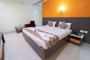 Quarto de hotel moderno com uma cama grande, mesa de cabeceira com telefone, uma cadeira vermelha e mesa de cabeceira com abajur.