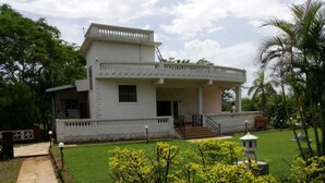 Um edifício de dois andares com varanda, varanda coberta e um gramado bem cuidado com plantas floridas em amarelo.