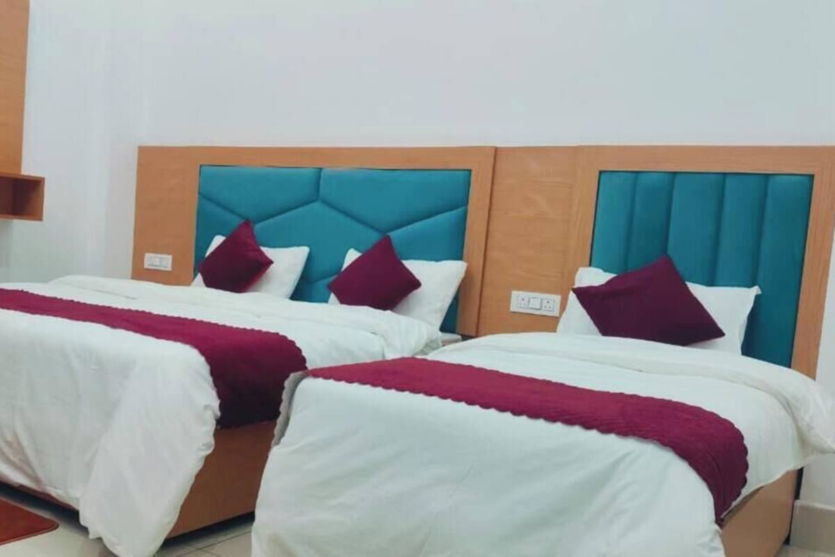 Duas camas com cabeceiras, roupa de cama branca e detalhes em vermelho.