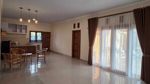 Uma sala de estar ampla com cozinha, mesa de jantar e cadeiras, janelas grandes com cortinas e piso revestido de azulejos.