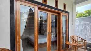 Quarto com porta de correr de vidro que dá para uma varanda, cadeiras de madeira e uma cama com vista.