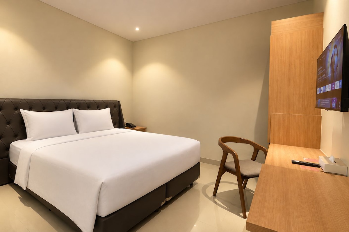 Um quarto moderno com uma cama grande, mesas de cabeceira, uma escrivaninha e uma televisão.
