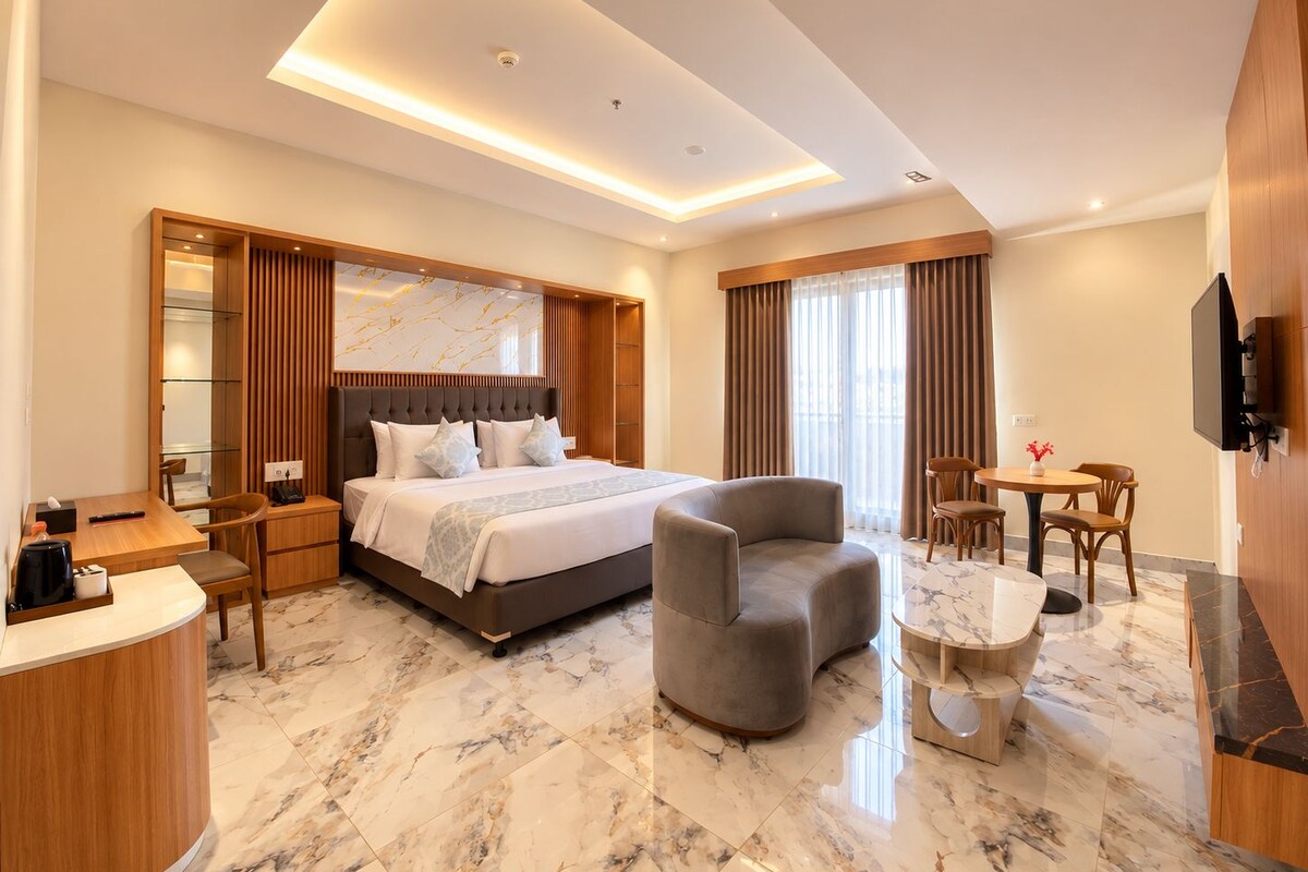 Quarto de hotel moderno com uma cama grande, uma escrivaninha, uma cadeira, uma TV e um espaço de banheiro.