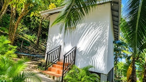 Um edifício branco com escadaria e corrimão, rodeado por vegetação exuberante e palmeiras.