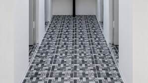 Um corredor estreito com piso de azulejos, um espelho redondo sobre uma pia e um claraboia.