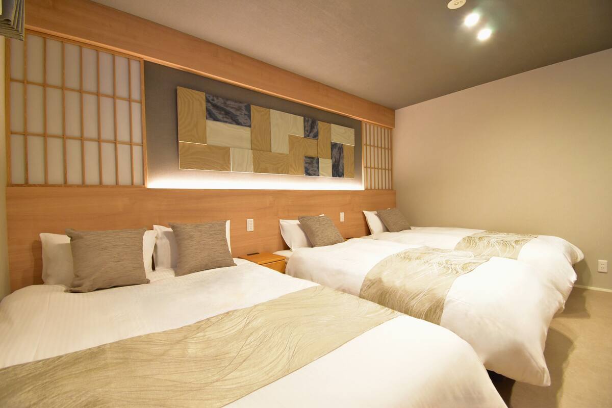 Quarto de hotel com duas camas, cabeceira de madeira, espelho fixado na parede e luz embutida no teto.