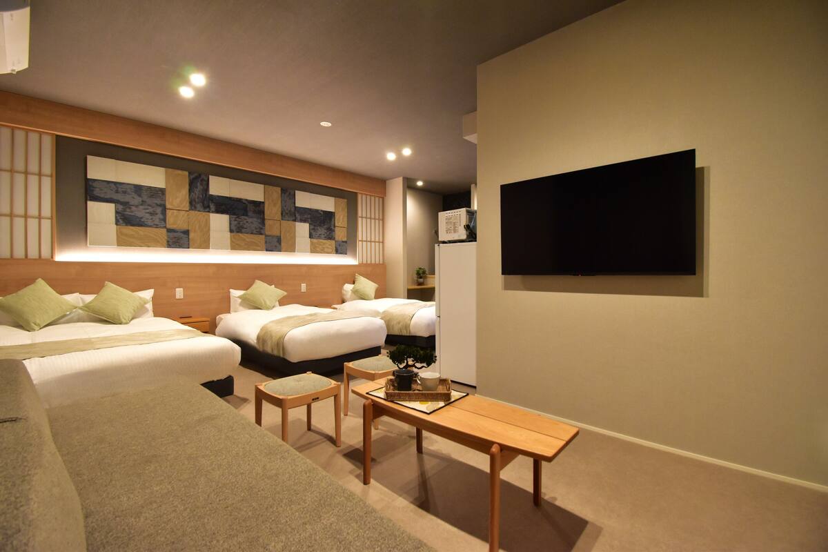 Quarto de hotel com duas camas, televisão, mesa de madeira e um painel decorativo na parede.