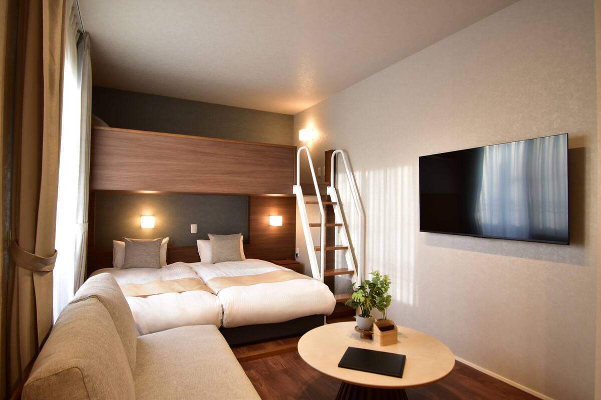 Quarto de hotel com cama, sofá, mesa redonda, televisão e escada.