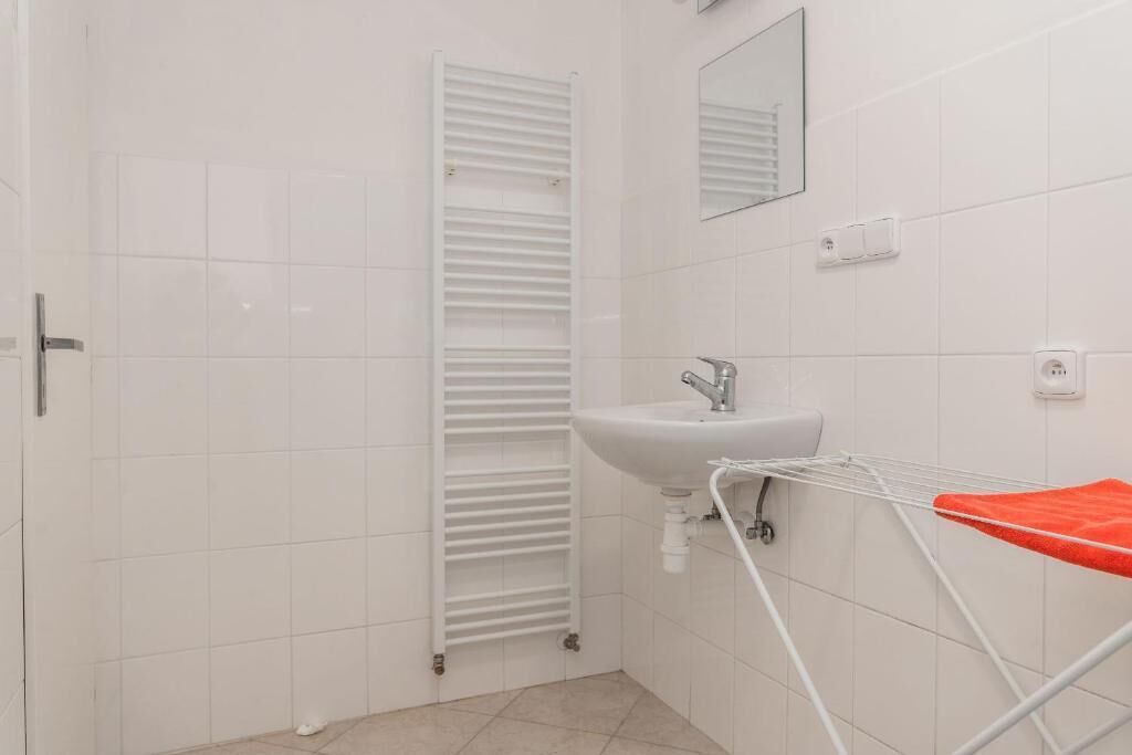 Casa de banho com azulejos brancos, uma pia branca, um espelho e um porta-toalhas com uma toalha vermelha.