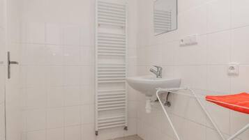 Casa de banho com azulejos brancos, uma pia branca, um espelho e um porta-toalhas com uma toalha vermelha.