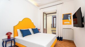 Quarto com cama, mesa de cabeceira, televisão e janela com cortinas.