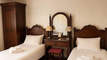 Quarto de hotel com duas camas, uma escrivaninha, um espelho e um guarda-roupa.