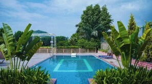Piscina com área central azul e límpida, rodeada por vegetação exuberante e uma estrutura de pérgula.