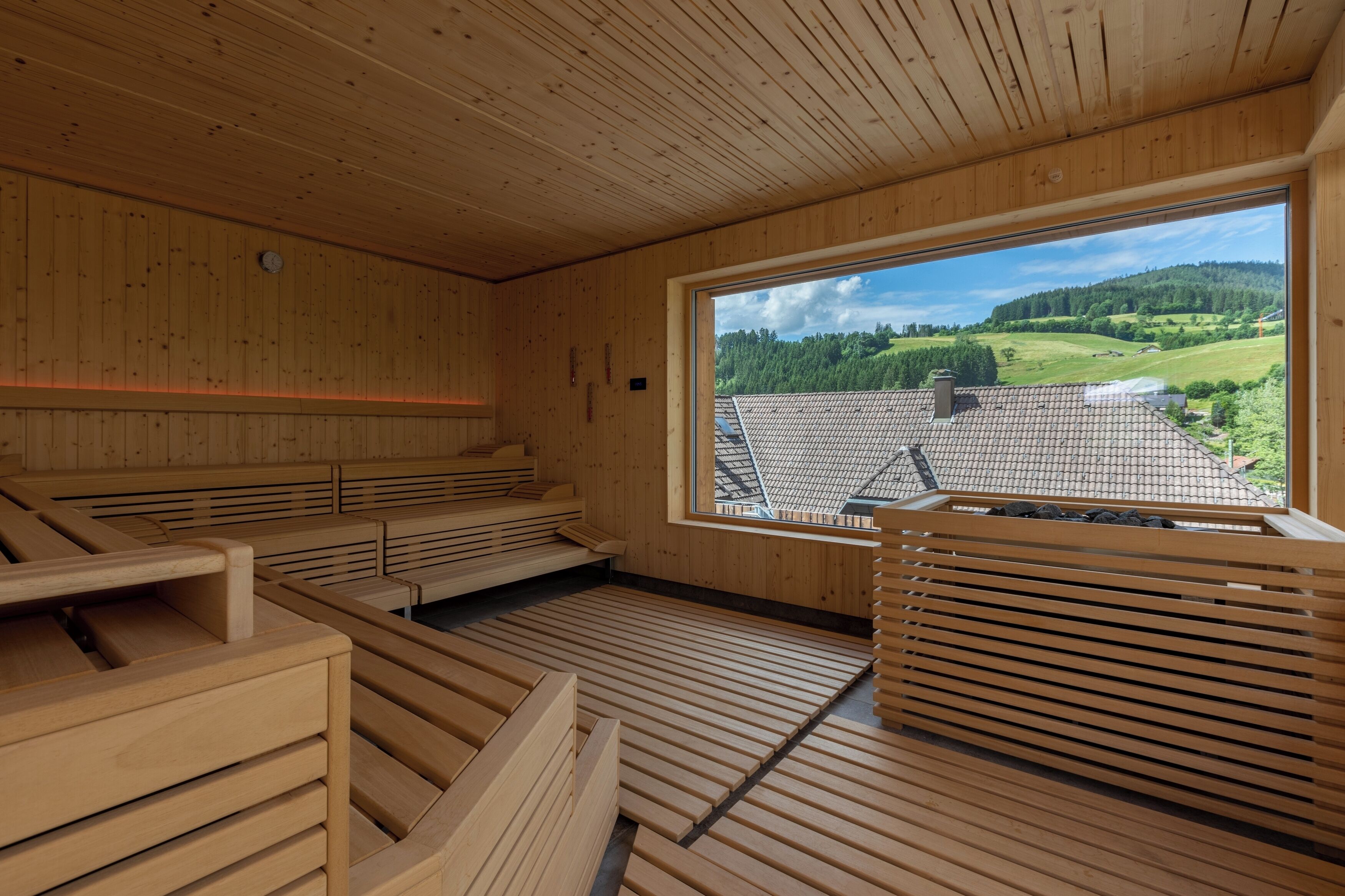 Sala de sauna com bancos de madeira e uma janela ampla com vista para uma paisagem verde.