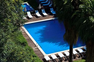 Piscina retangular com deck de madeira e espreguiçadeiras brancas.