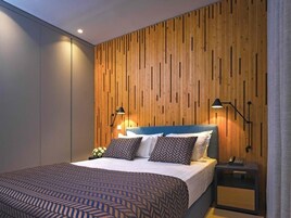 Quarto moderno com parede de painel de madeira, cama com roupa de cama estampada, duas luminárias de cabeceira e mesa de cabeceira com um telefone.