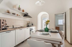 Uma cozinha moderna com armários brancos, uma mesa de jantar posta para quatro pessoas e vista para o quarto adjacente através de um arco.