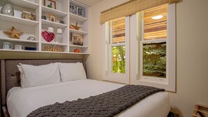 Um quarto com uma cama, uma estante com objetos decorativos e uma janela com vista para árvores.