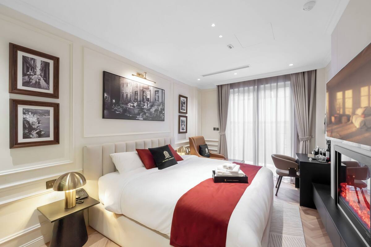 Quarto de hotel com uma cama grande, uma escrivaninha, uma televisão e quadros nas paredes.