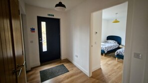 Corredor que leva a um quarto com uma cama, uma porta com um aviso e um acessório de iluminação.