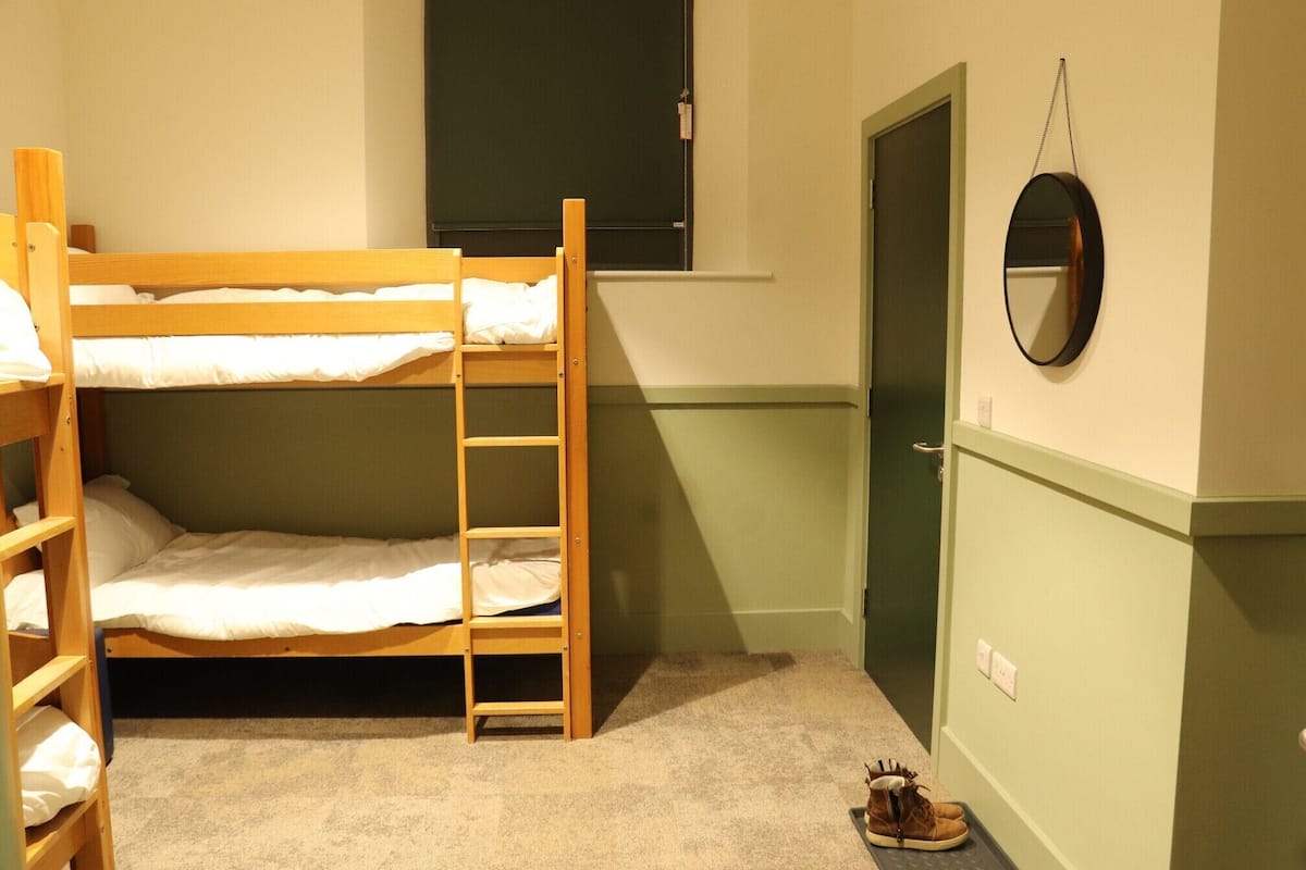 Quarto com beliche, escada, porta, espelho e um par de sapatos no chão.