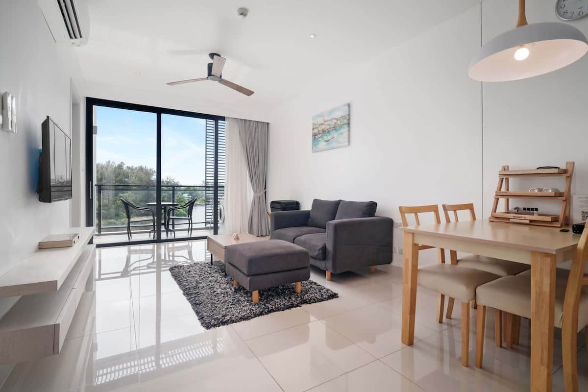 Uma sala de estar moderna com sofá, banquinho, mesa de jantar, cadeiras e ventilador de teto.