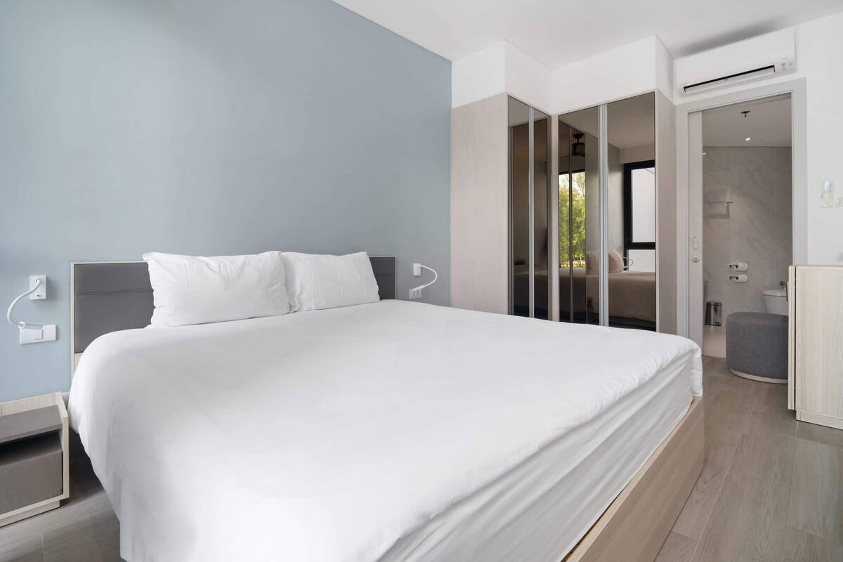 Quarto de hotel moderno com uma cama grande, um closet amplo e banheiro com chuveiro e vaso sanitário.