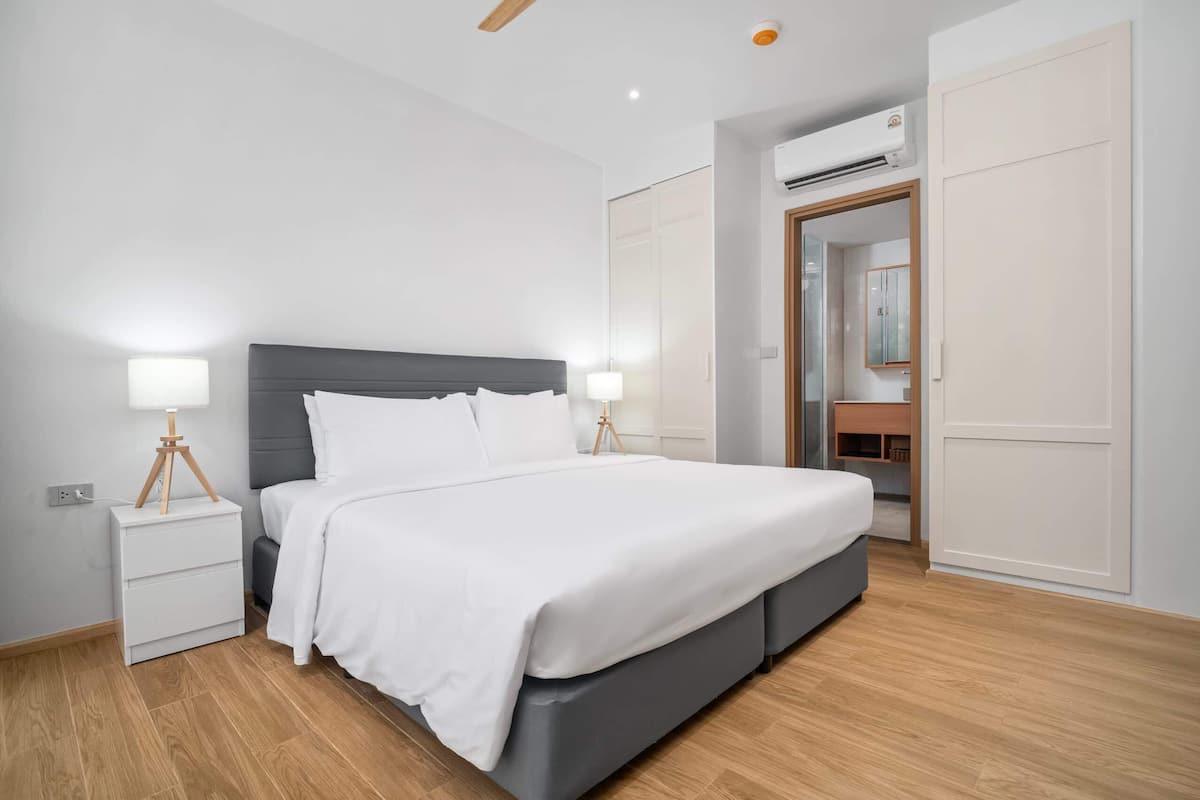 Quarto moderno com cama, luminárias de cabeceira, mesa de cabeceira e aparelho de ar condicionado.