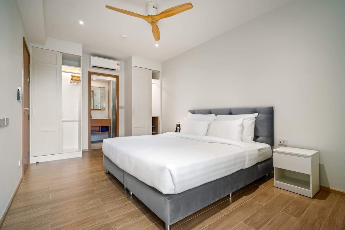 Um quarto moderno com uma cama grande, um ventilador de teto e uma mesa de cabeceira branca.