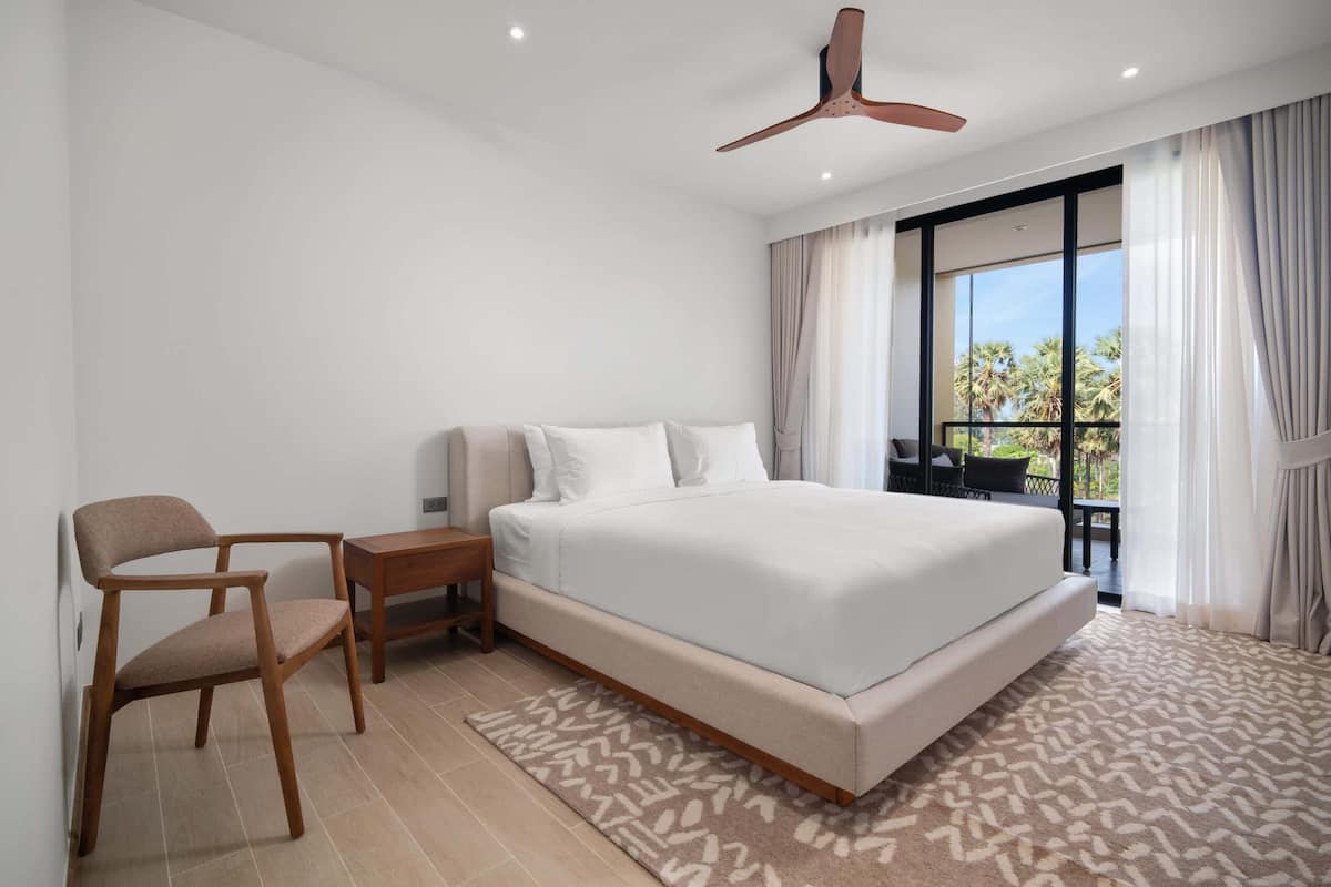 Quarto com uma cama grande, uma cadeira, uma mesinha de cabeceira e um ventilador de teto.