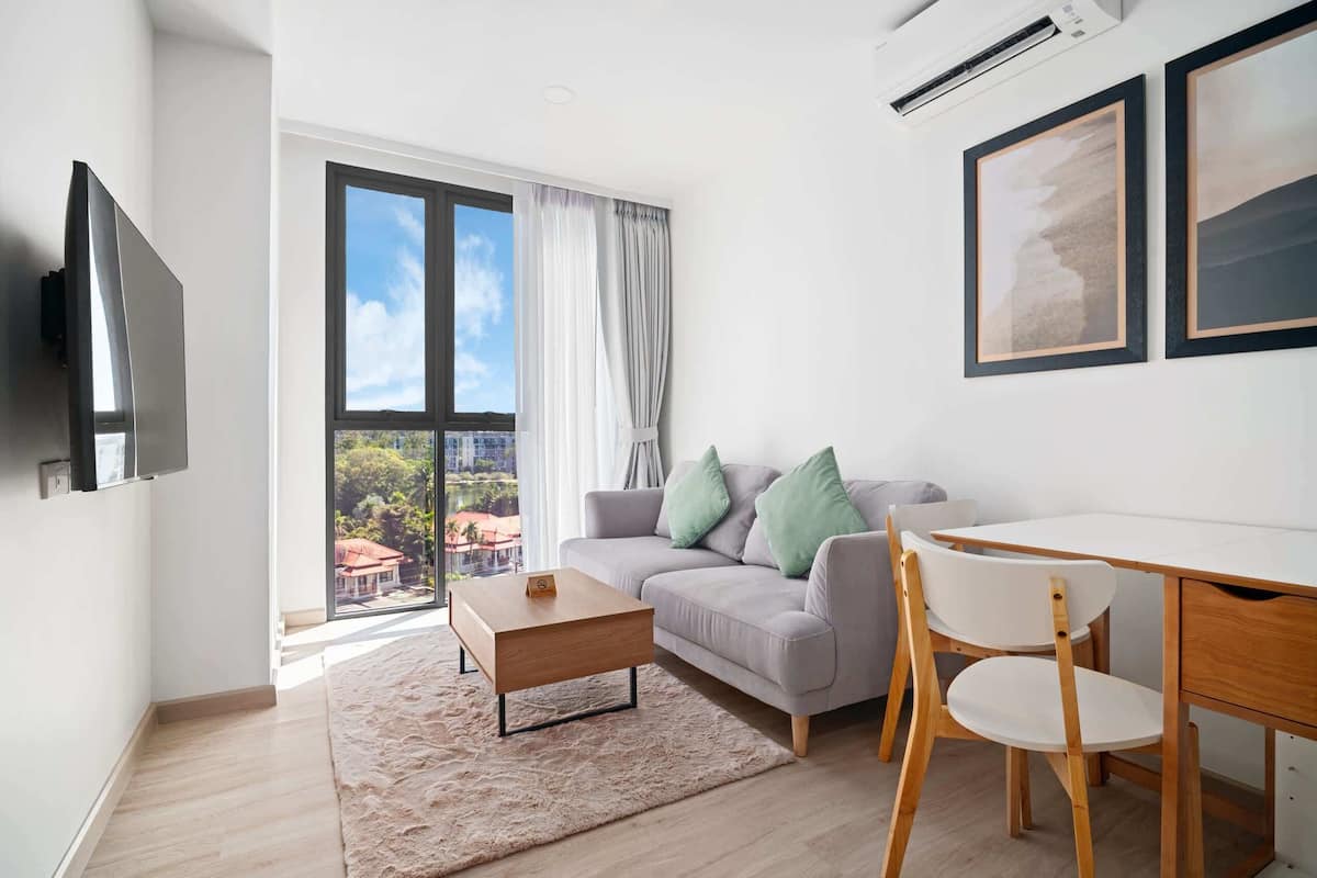Uma sala de estar moderna com sofá, mesa de centro de madeira, escrivaninha e televisão na parede.