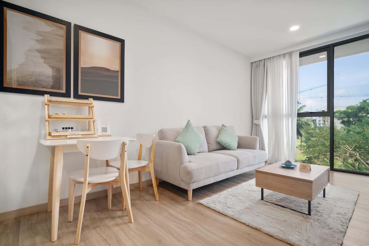 Uma sala de estar moderna com sofá, mesa de centro e escrivaninha com cadeiras. Há duas imagens emolduradas na parede.