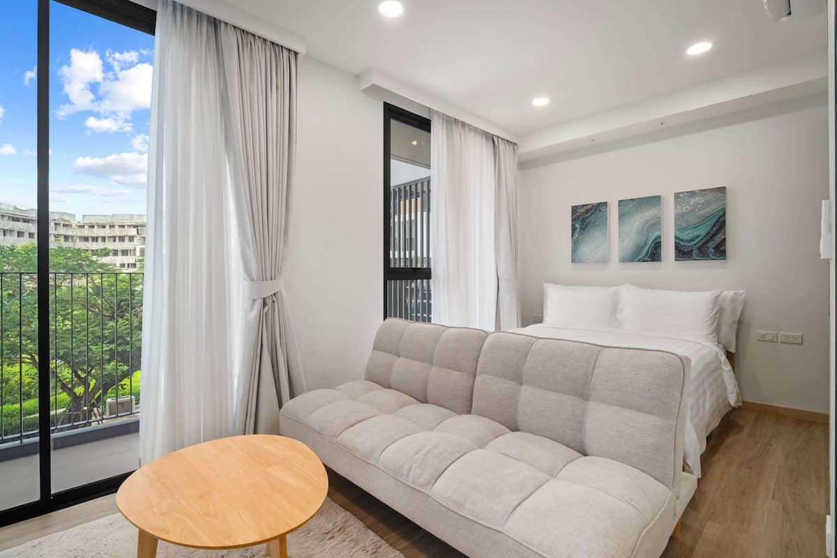 Quarto moderno com sofá-cama, uma pequena mesa de madeira e uma grande janela com cortinas.