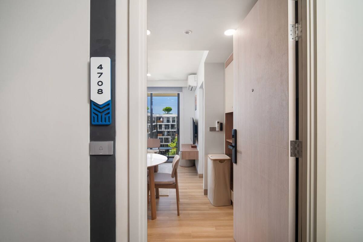 Um corredor moderno com uma porta identificada como '4708', uma área de jantar com mesa e cadeiras, e vista para um edifício lá fora.