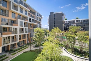 Um edifício residencial com vários andares, varandas, um pátio com vegetação e céu claro.