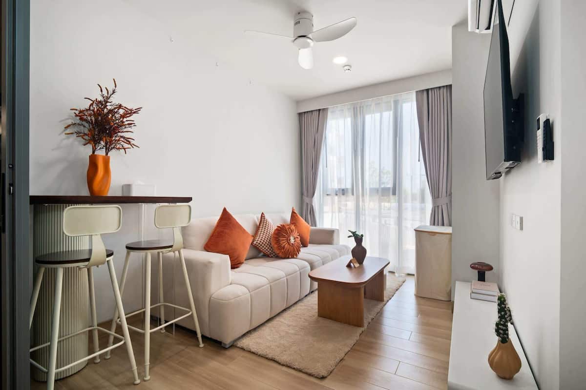 Uma sala de estar moderna com um sofá, dois banquetes, uma mesa de centro, uma TV fixada na parede e um ventilador de teto.